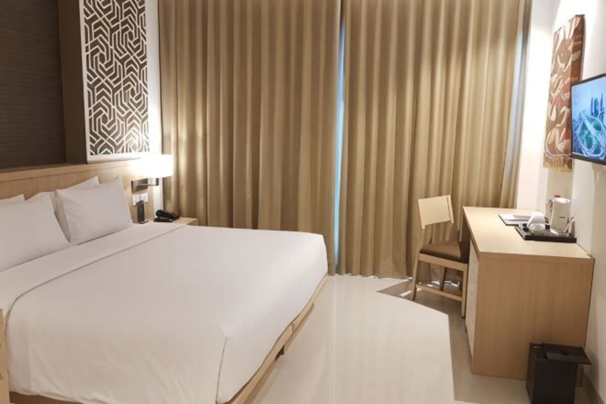 Quarto de hotel com uma cama grande, uma escrivaninha, uma cadeira, uma televisão e cortinas.