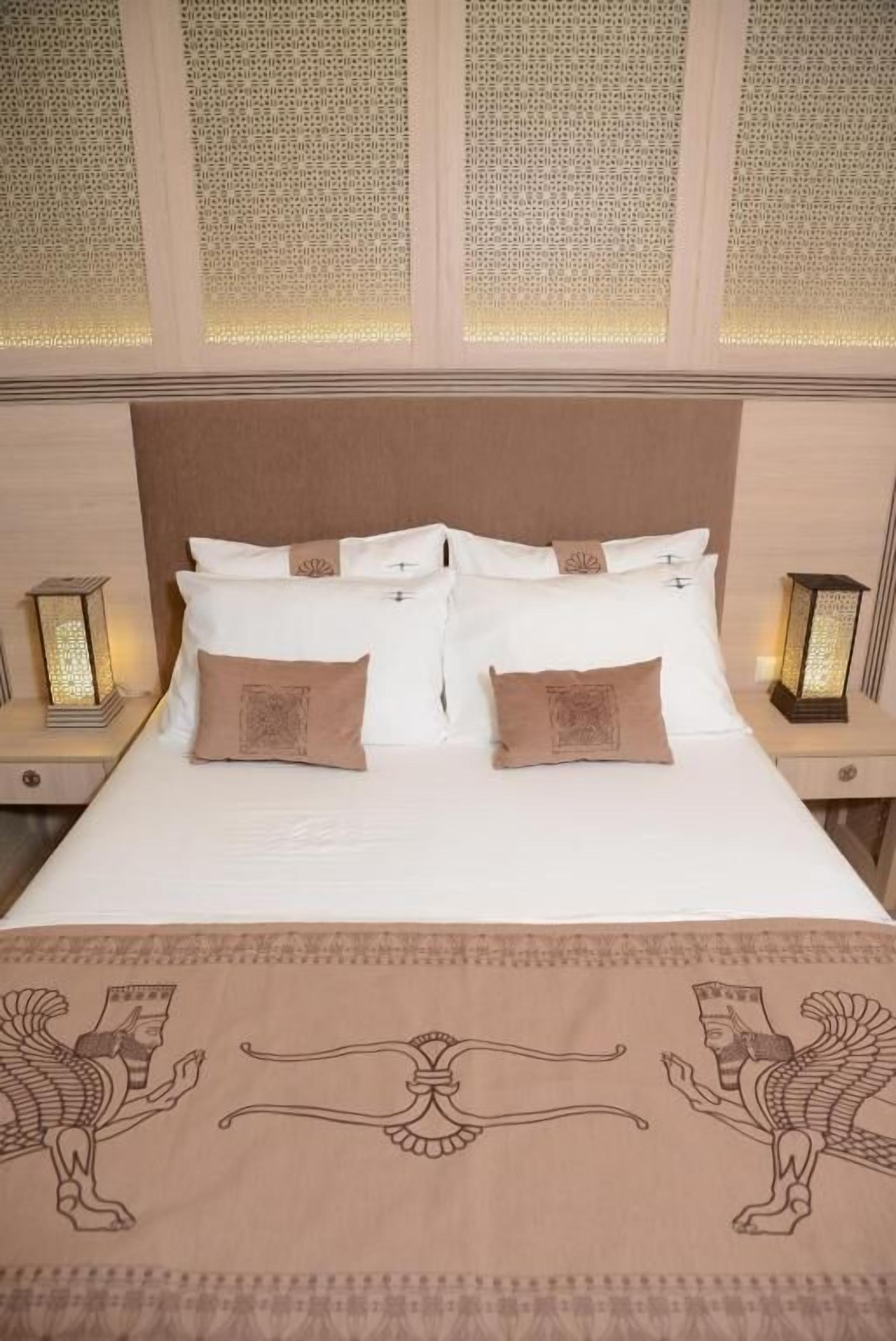 Cama bem arrumada com cabeceira marrom, lençóis brancos e almofadas decorativas.