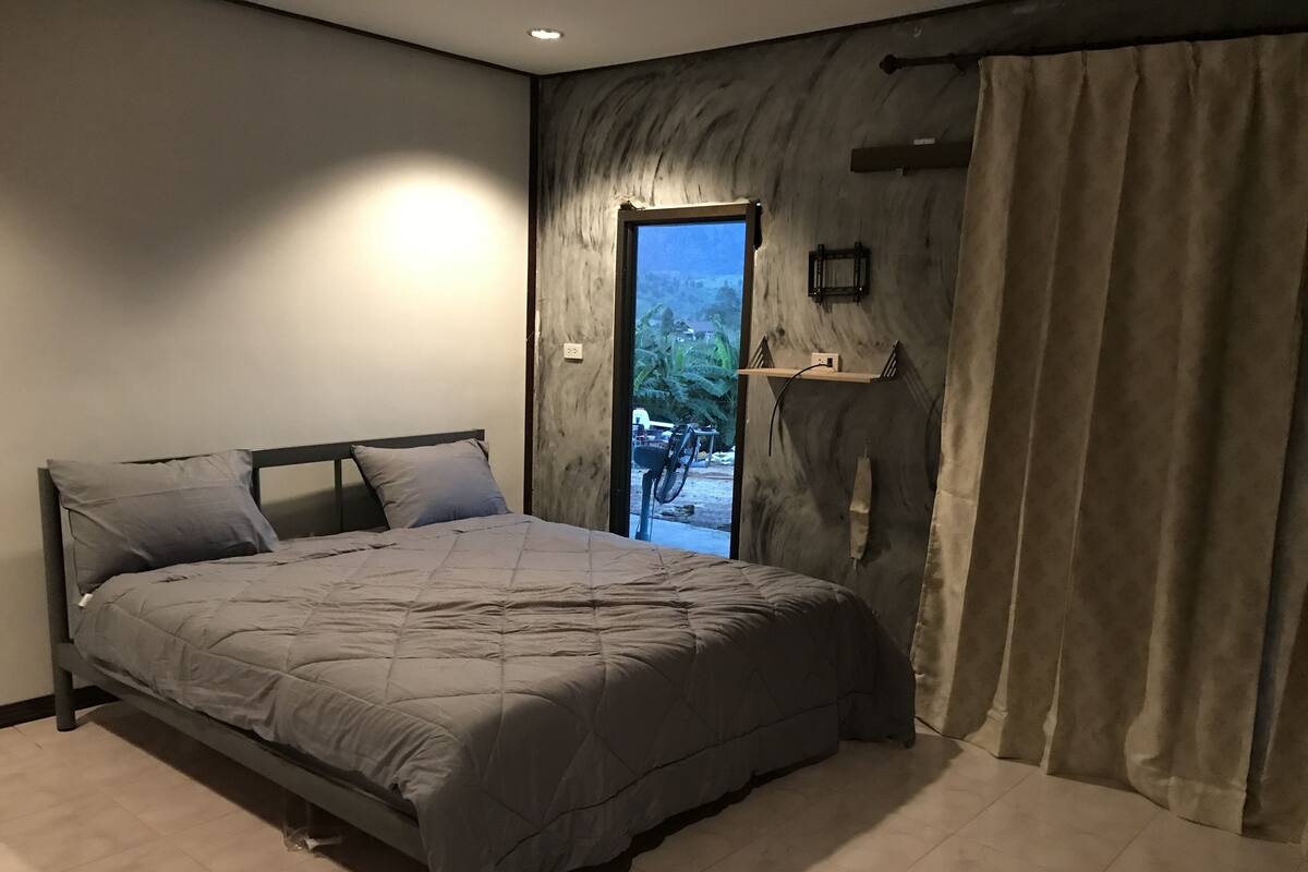 Quarto com cama, janela, porta e cortina.