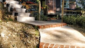 Uma casa com escadaria que dá para um deck de madeira, cercada por árvores e plantas.