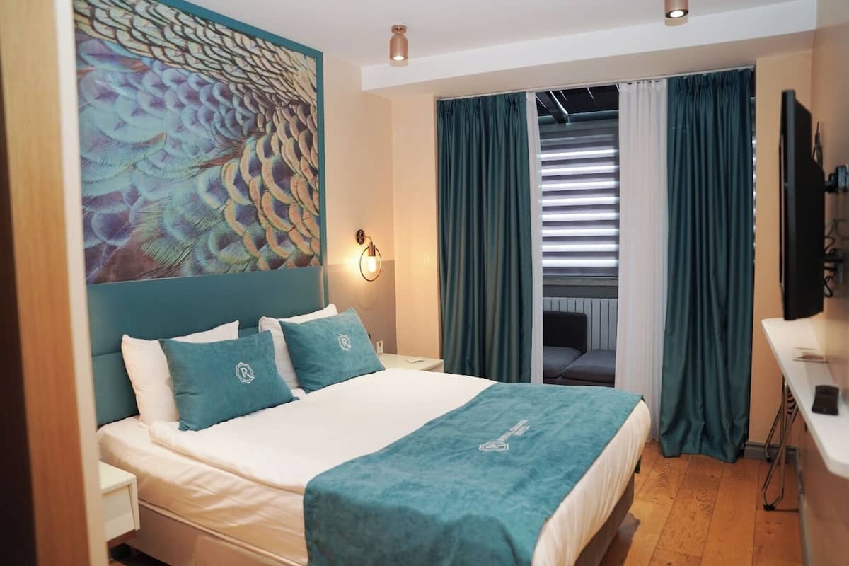 Quarto de hotel com uma cama, um quadro na parede, uma escrivaninha e uma televisão.