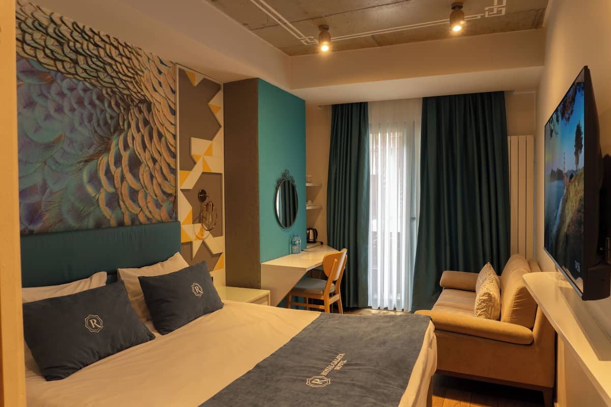 Quarto de hotel com uma cama, uma escrivaninha, um sofá, uma televisão e um quadro na parede.