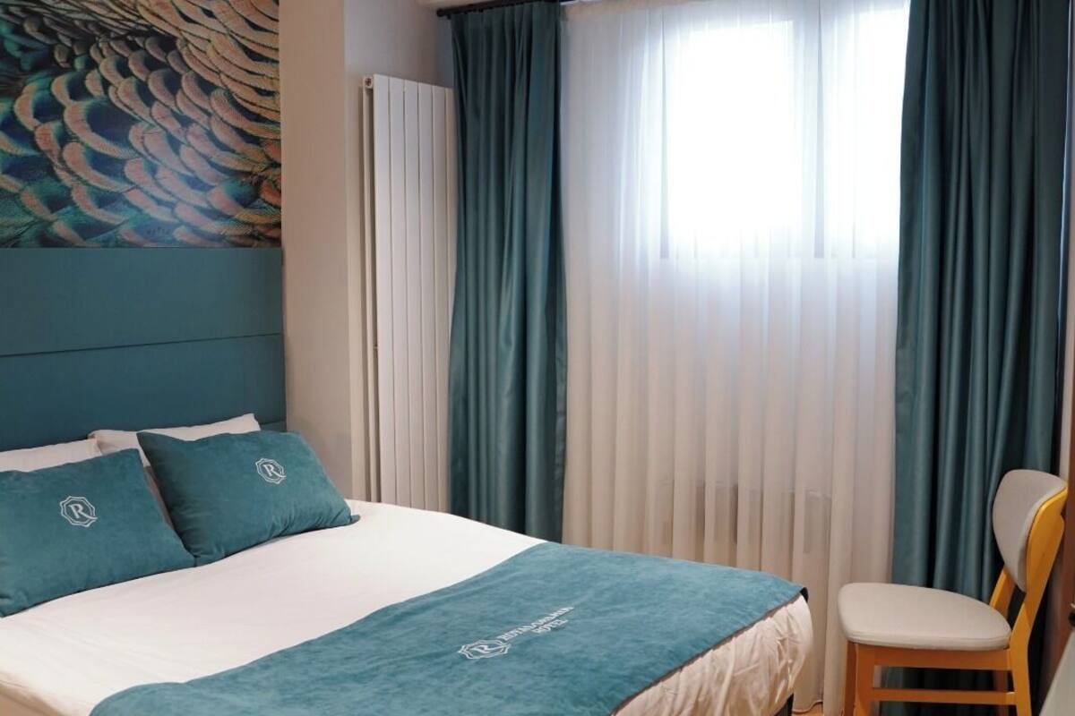 Um quarto com cama, cadeira, janela com cortinas e parede com padrão de pena de pavão.