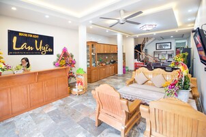 Uma sala de estar ampla com um balcão de recepção em madeira, um conjunto de sofás e uma área de cozinha.