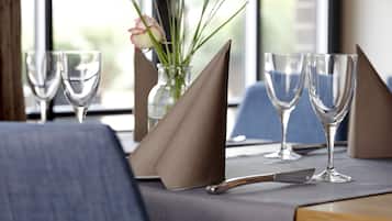 Mesa posta com copos de vinho transparentes, uma faca e um vaso com uma flor.