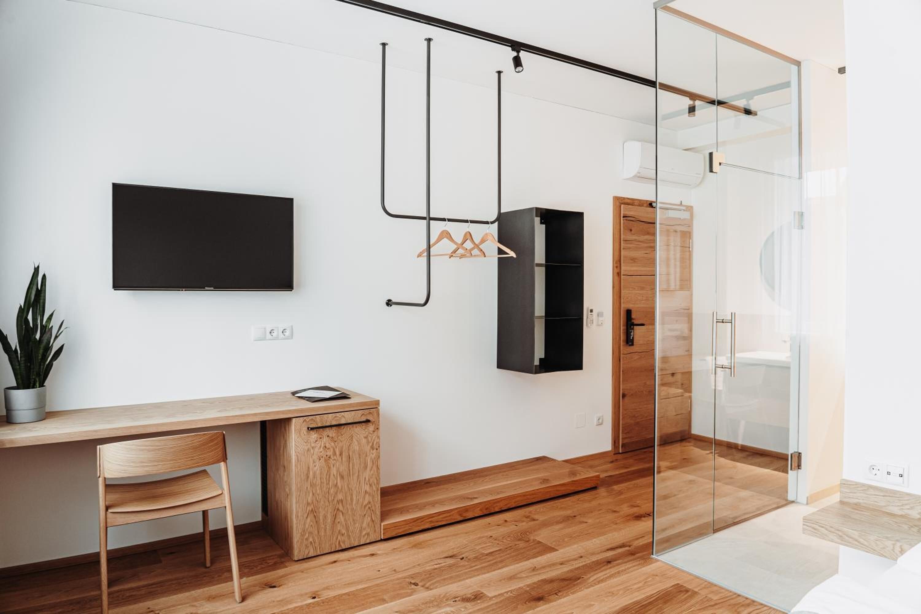 Quarto moderno com escrivaninha de madeira, TV fixada na parede, guarda-roupa e box de chuveiro de vidro.
