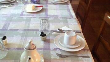 Mesa de jantar posta com pratos, xícaras e um bule, indicando um ambiente para refeições.