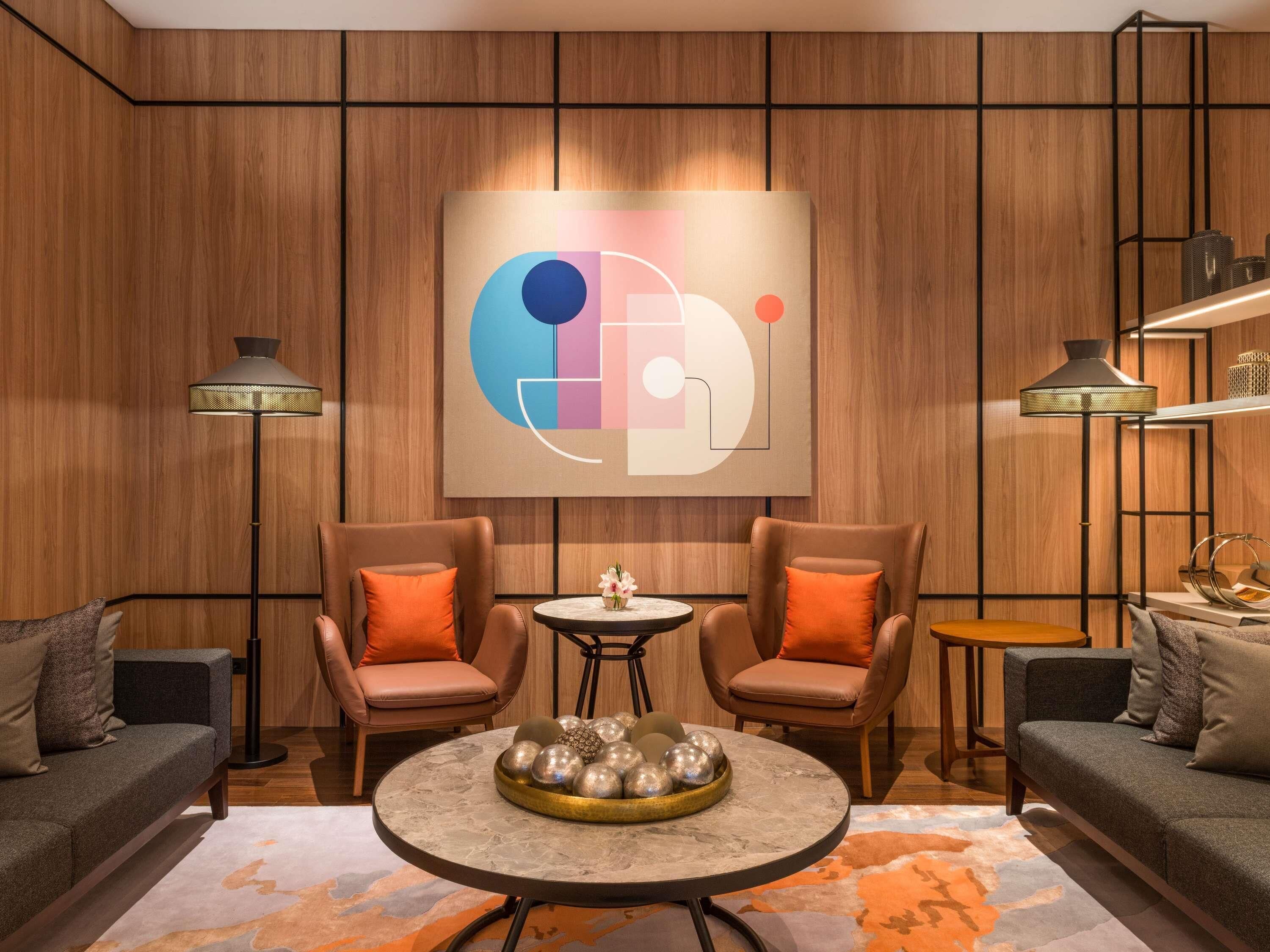 Quarto moderno com duas poltronas de couro, uma mesa de centro redonda com objetos decorativos e uma grande pintura abstrata na parede.