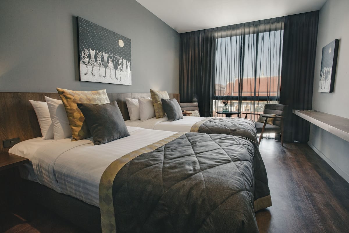 Quarto de hotel com duas camas, uma mesa e uma janela grande com cortinas.
