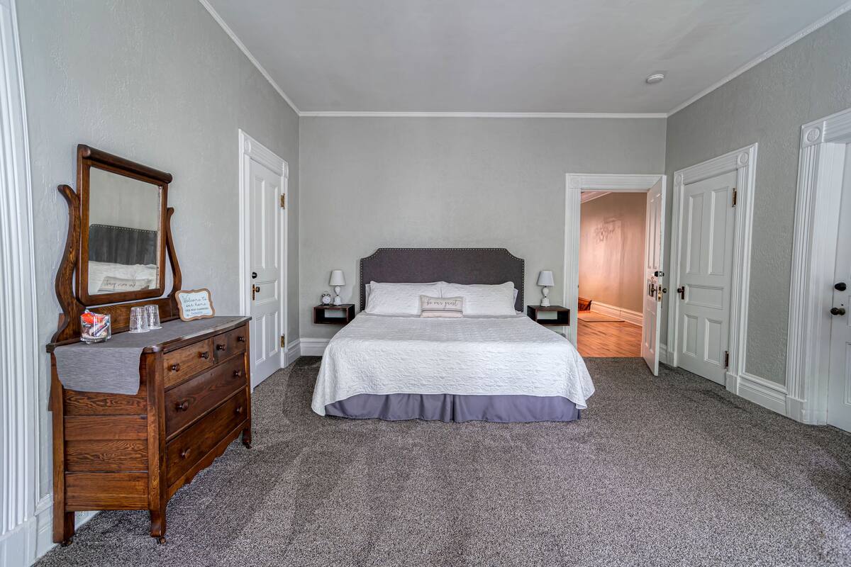 Quarto com uma cama grande, cômoda, espelho e duas mesas de cabeceira.