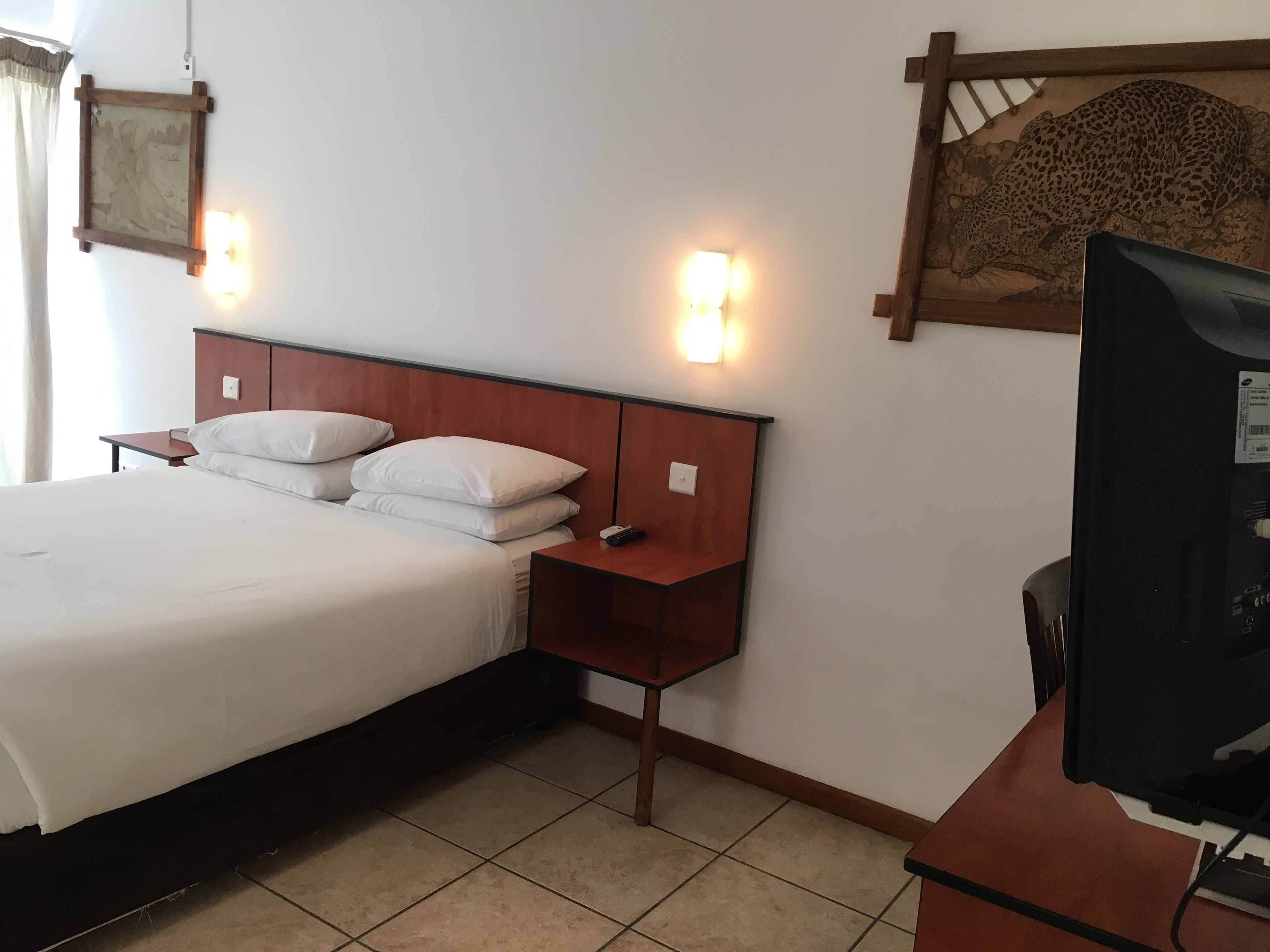 Quarto de hotel com cama, mesas de cabeceira, televisão e uma obra de arte na parede.