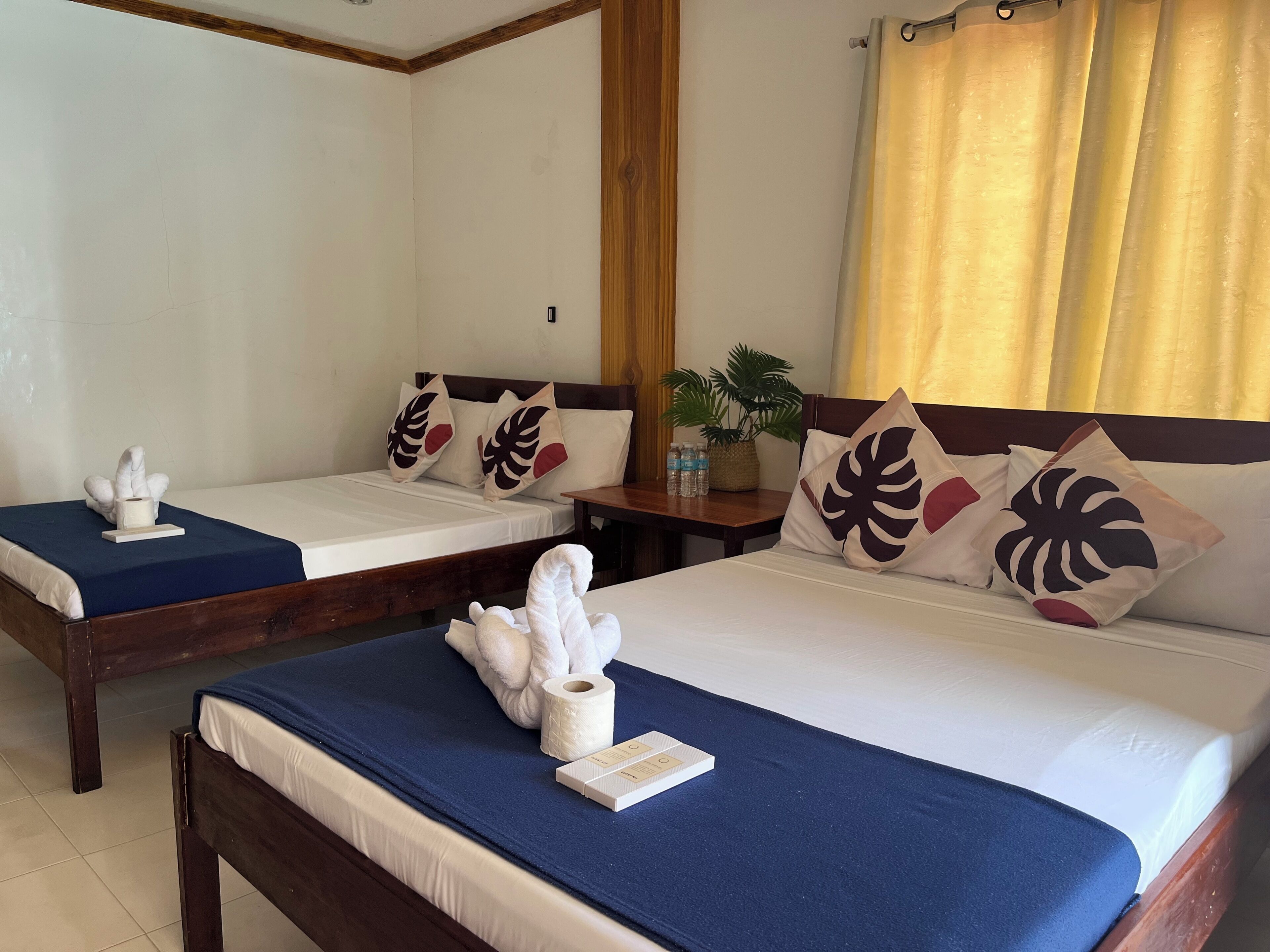 Duas camas de solteiro com estruturas de madeira, roupa de cama branca e almofadas decorativas.