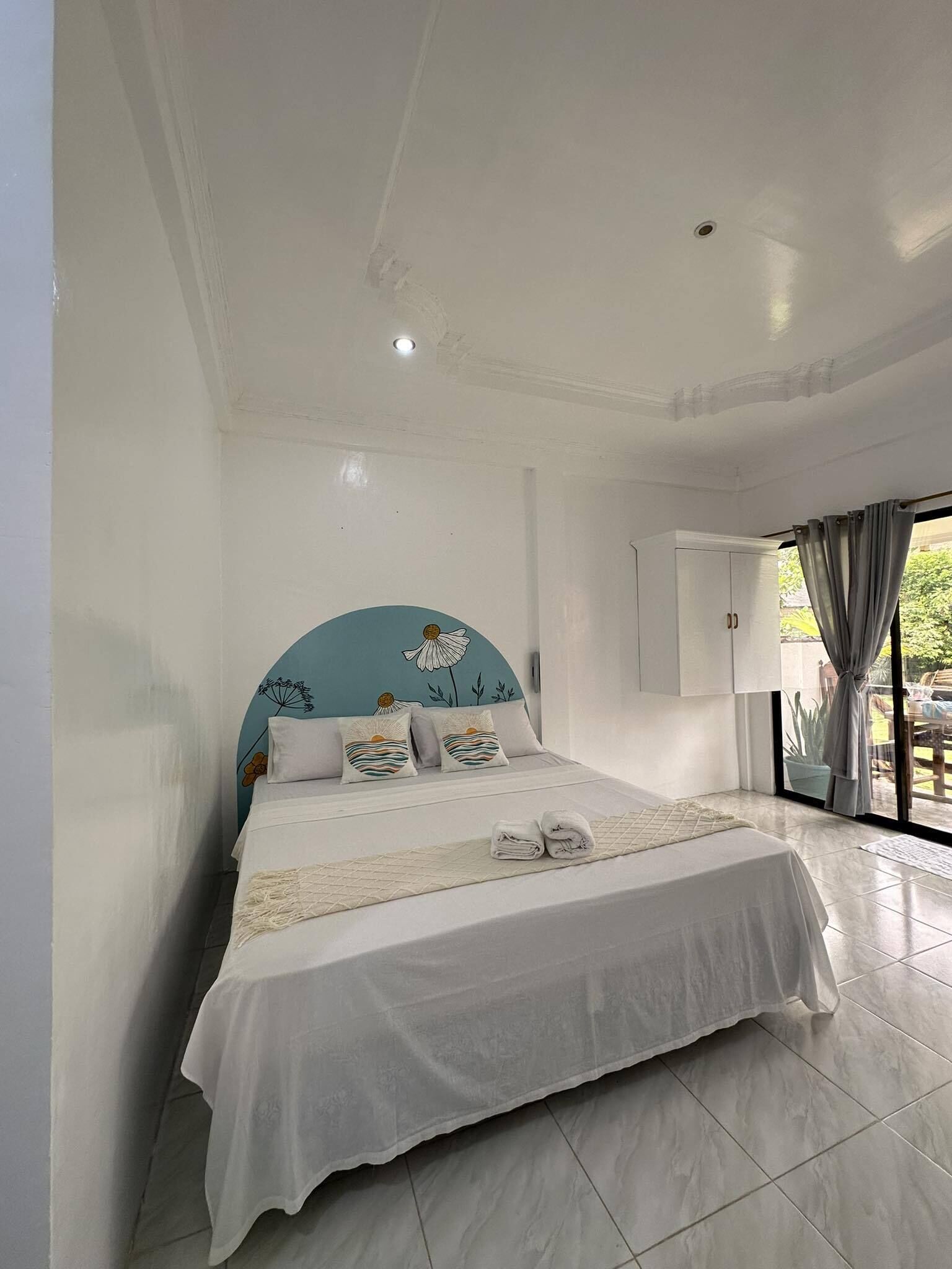 Um quarto com uma cama grande, um ventilador de teto, uma janela com cortinas e vista para o exterior.