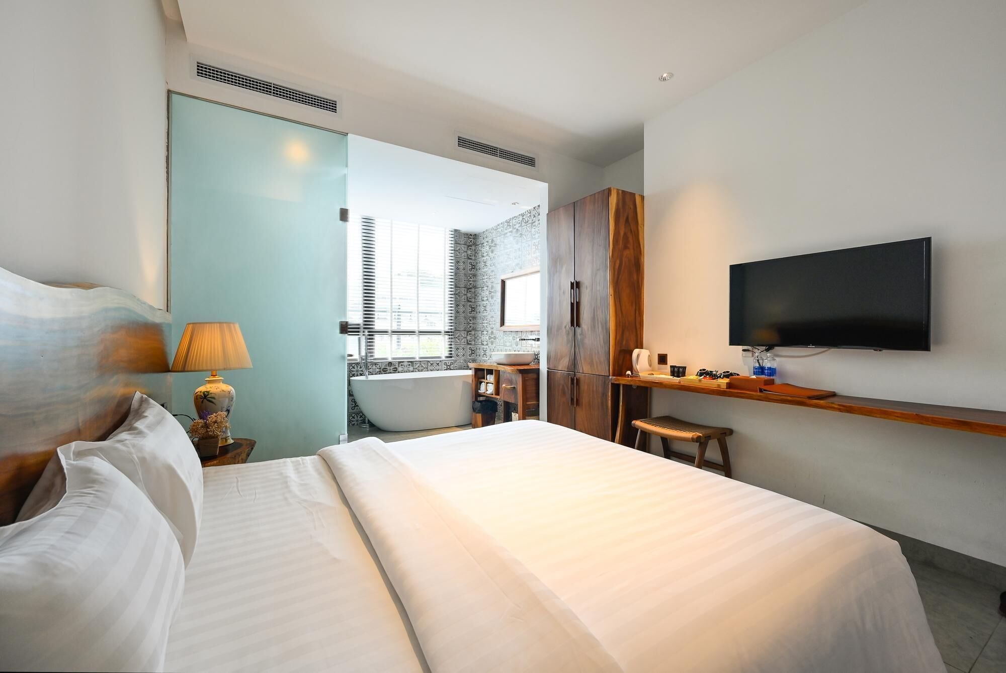 Quarto de hotel com cama, televisão na parede, casa de banho com banheira e janela com persianas.