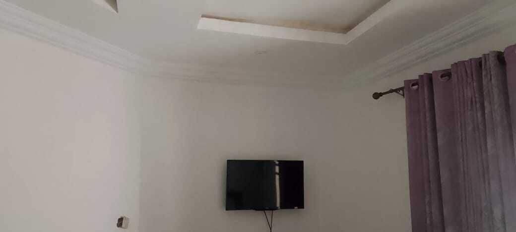 Quarto com televisão de tela plana na parede, teto com design rebaixado e cortina roxa à direita.