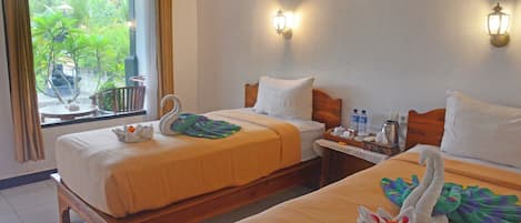 Quarto de hotel com duas camas, uma janela com cortinas, um quadro na parede e uma mesa com artigos de higiene pessoal.