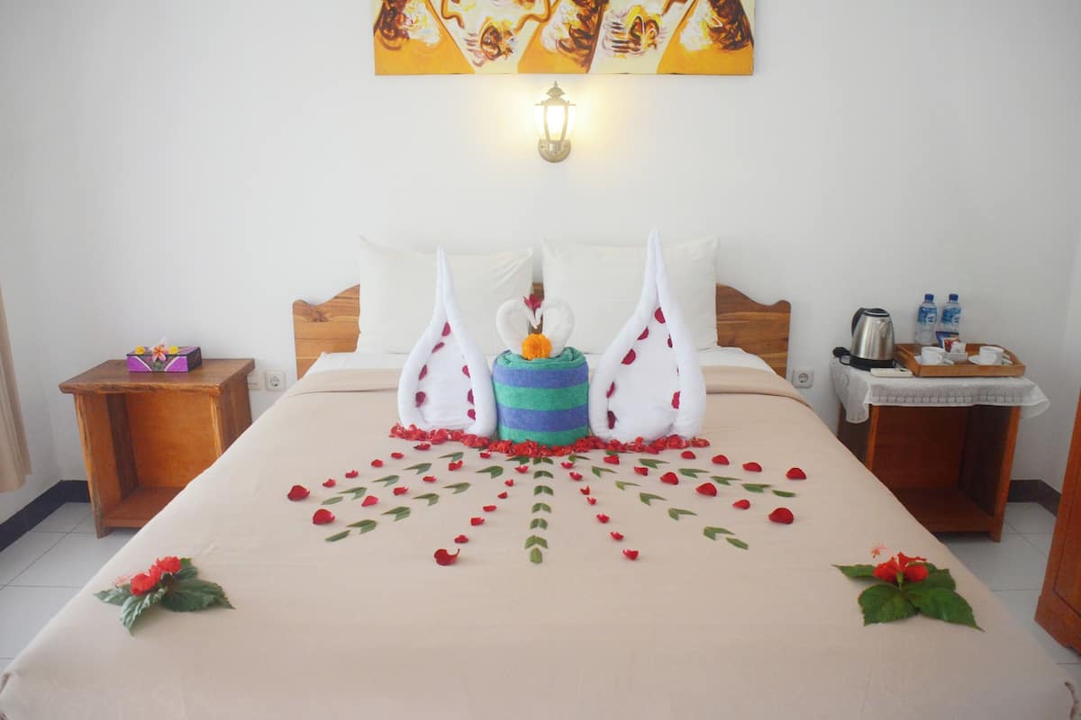 Quarto de hotel com cama, almofadas, mesa de cabeceira, abajur e uma parede com obras de arte.