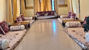 Um hall amplo com teto alto, diversas áreas de estar e um lustre central.