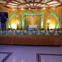 Um palco com um fundo dourado em tecido drapeado, um sofá branco e arranjos florais.