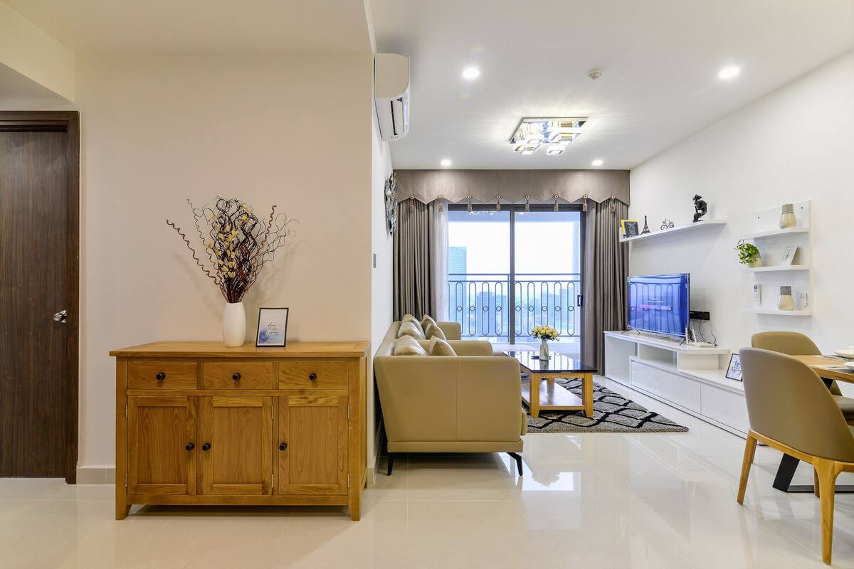 Uma sala de estar moderna com um sofá, um armário de madeira, uma televisão e uma varanda com vista.