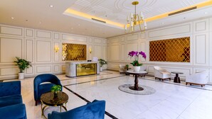 Um hall amplo com piso de mármore, balcão de recepção e áreas de estar com cadeiras azuis e brancas.