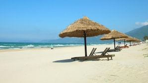 Uma praia com guarda-sóis de palha e cadeiras de praia.