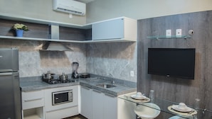 Cozinha moderna com fogão embutido, micro-ondas e pia. Há uma TV fixada na parede e uma pequena área de estar com banquetas.