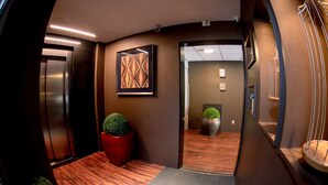 Um corredor moderno com piso de madeira, um vaso com planta e uma obra de arte emoldurada na parede.