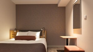 Quarto de hotel com cama bem arrumada, mesa de cabeceira com luminária e um pequeno banquinho.