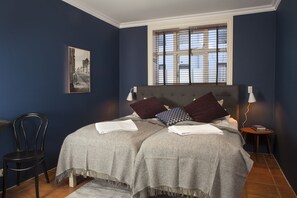 Quarto com uma cama grande, duas luminárias de cabeceira, uma cadeira e uma janela com persianas.