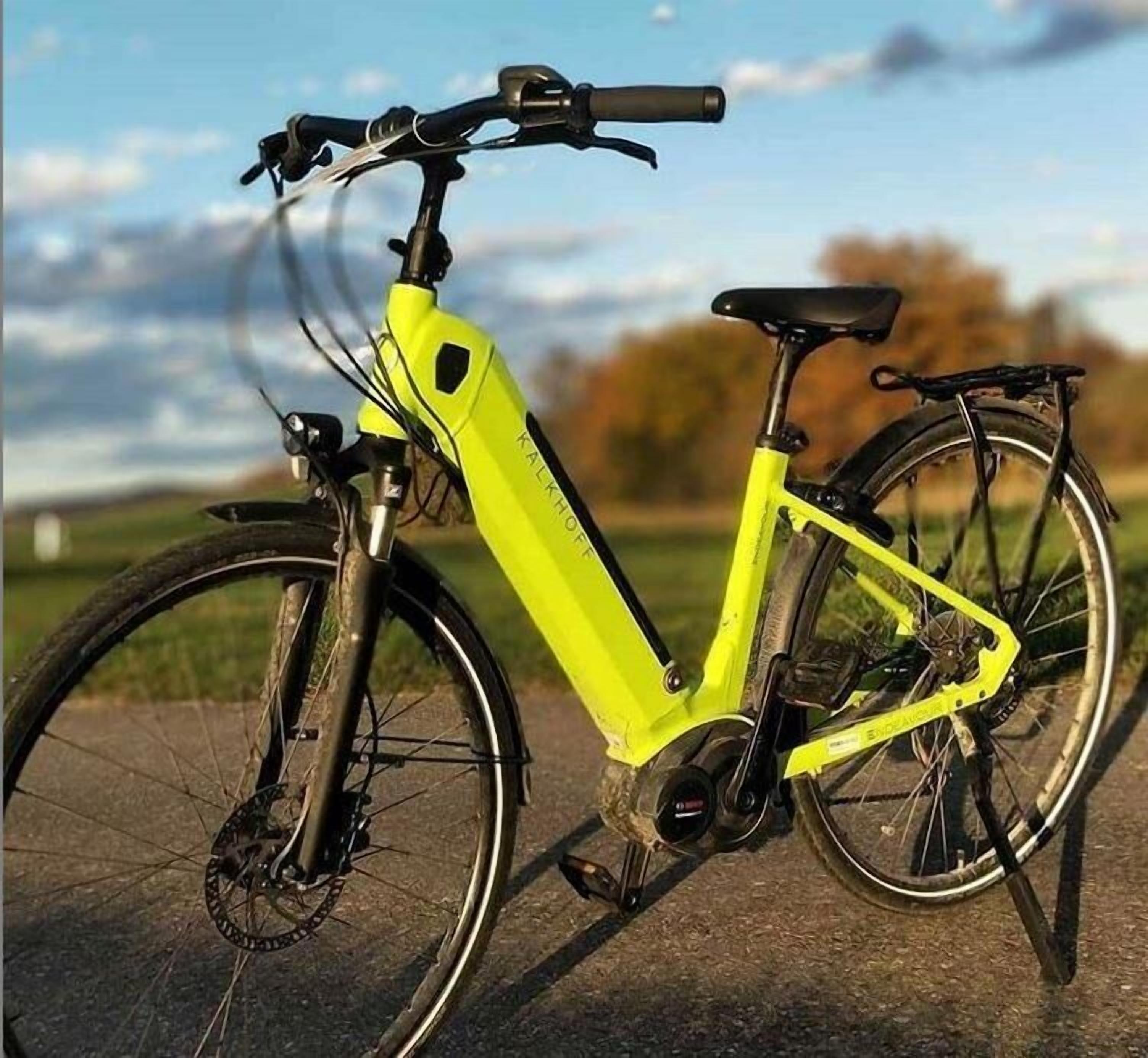 Uma bicicleta elétrica amarela estacionada em um caminho pavimentado, com céu azul ao fundo.