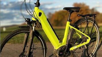 Uma bicicleta elétrica amarela estacionada em um caminho pavimentado, com céu azul ao fundo.
