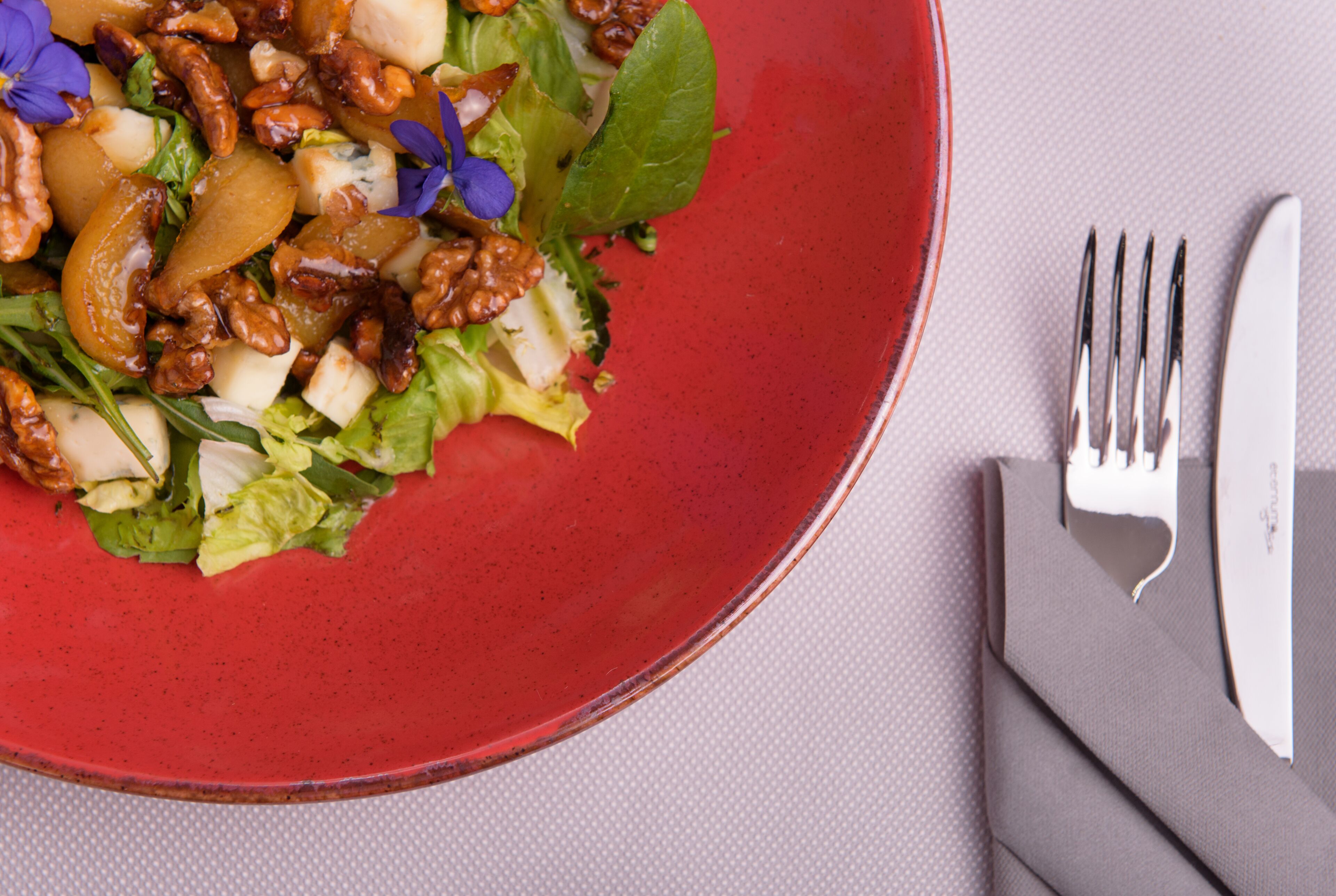 Prato vermelho com salada, um garfo e uma faca sobre a mesa.