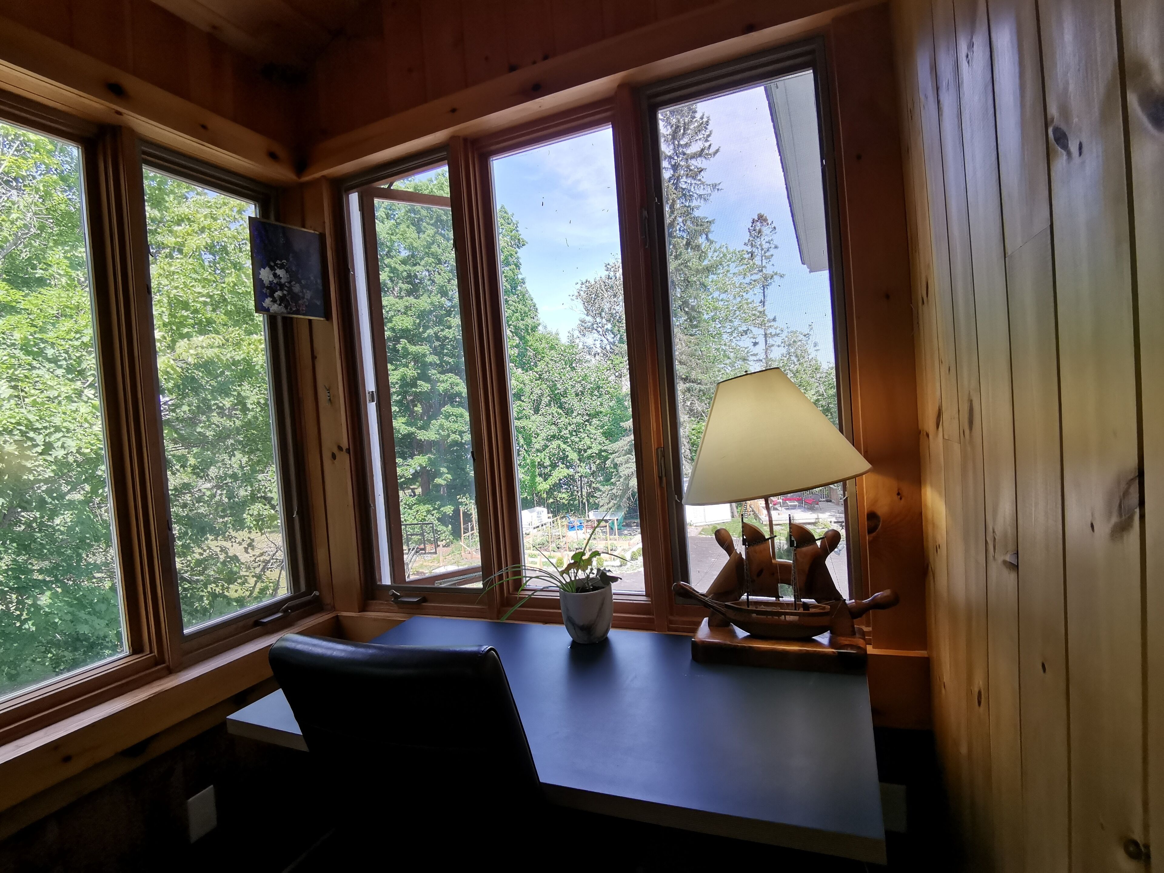 Interior de uma cabana com mesa de jantar, cadeiras, uma luminária e vista para árvores através de grandes janelas.