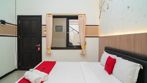 Cama bem arrumada com colcha vermelha e branca, travesseiro com detalhe vermelho e toalha ao lado.