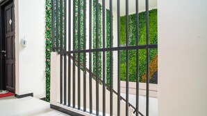Uma escadaria com corrimão de metal, uma porta e uma parede com folhagem verde.