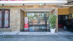 Entrada de hotel com tapete de boas-vindas, planta em vaso e placa da RedDoorz.