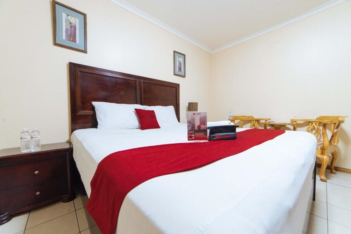 Quarto de hotel com uma cama grande, uma mesa de cabeceira de madeira, uma mesa e uma cadeira.