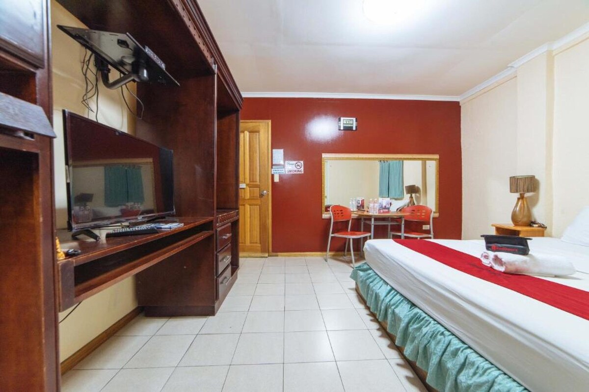 Quarto de hotel com cama, escrivaninha com computador, televisão e área de refeições com cadeiras e mesa.