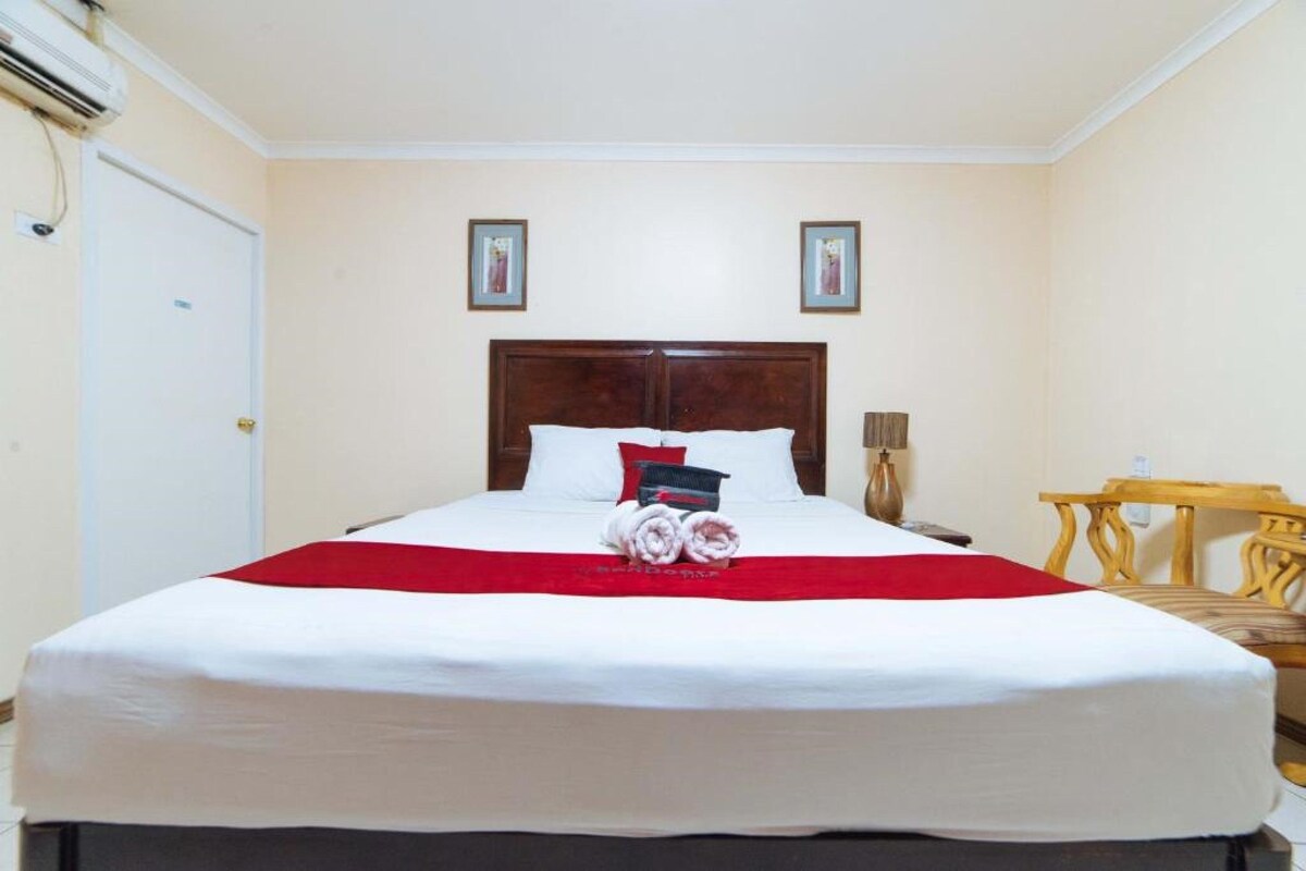 Uma cama bem arrumada com um cobertor vermelho, travesseiros brancos e um arranjo de flores.