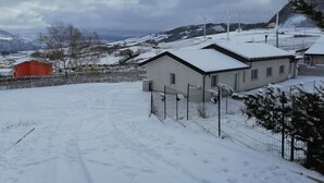 Um bairro residencial com casas cobertas de neve, um quintal cercado e um prédio vermelho ao fundo.