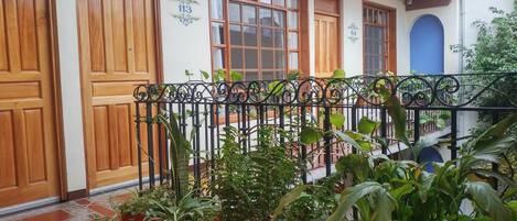 Um edifício com portas numeradas, uma varanda e vasos de plantas.