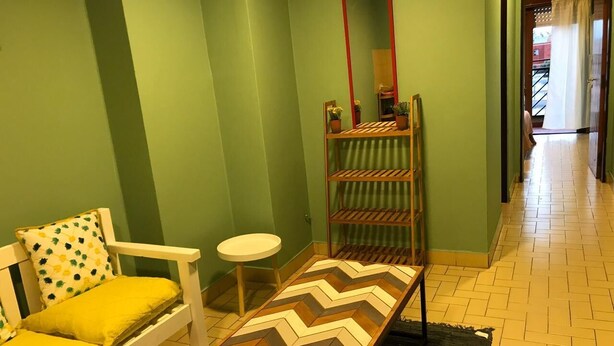 Quarto com cama, uma mesinha redonda, um banco e um espelho na parede.