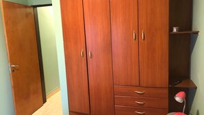 Um quarto com um guarda-roupa de madeira, uma escrivaninha pequena e um abajur rosa.