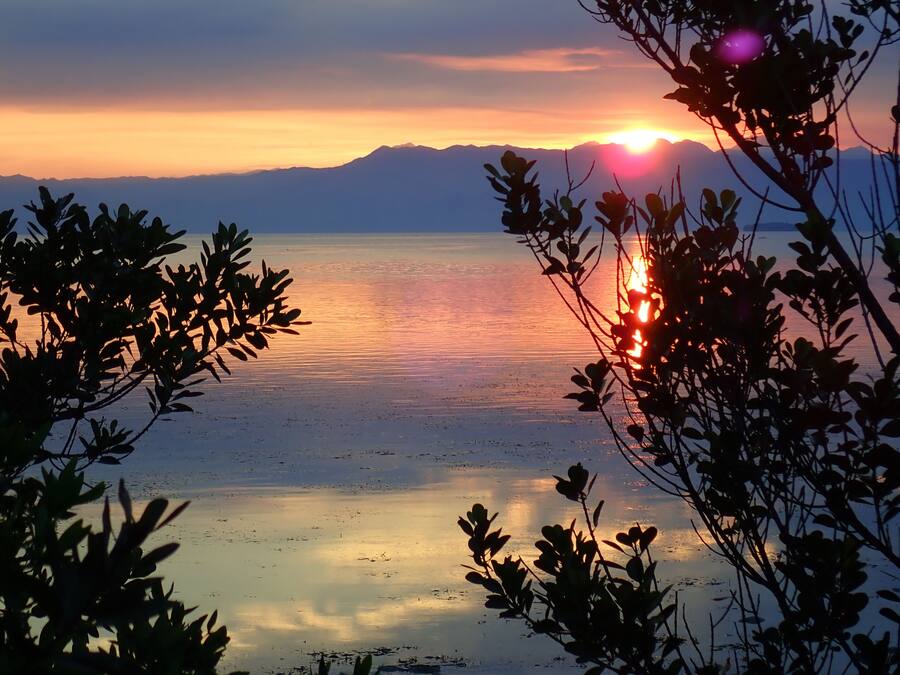 Um pôr do sol sobre águas calmas, com montanhas ao fundo.