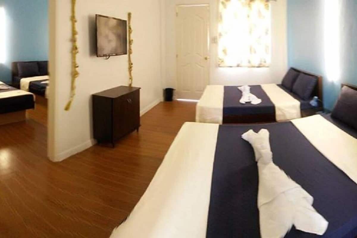 Quarto de hotel com duas camas, televisão, guarda-roupa e janela com cortinas.