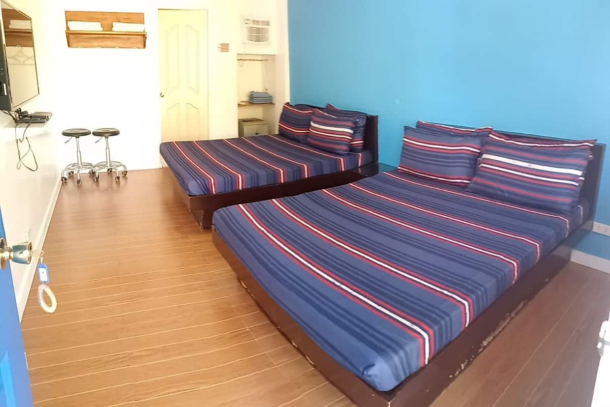 Quarto com duas camas, piso de madeira, parede azul, porta e uma pequena mesa com bancos.
