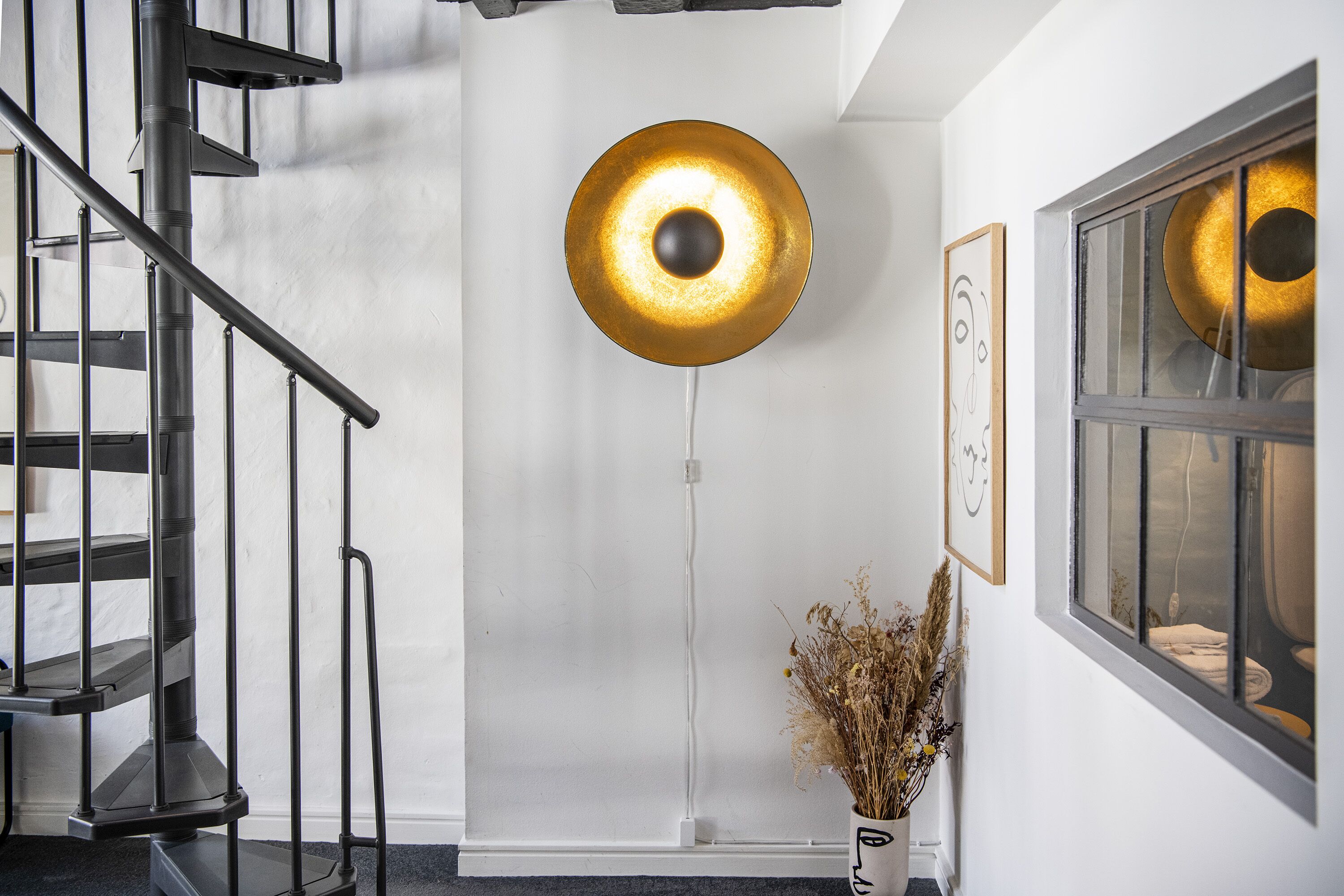 Uma escadaria com corrimão preto, luminária fixada na parede e janela com vista para o exterior.