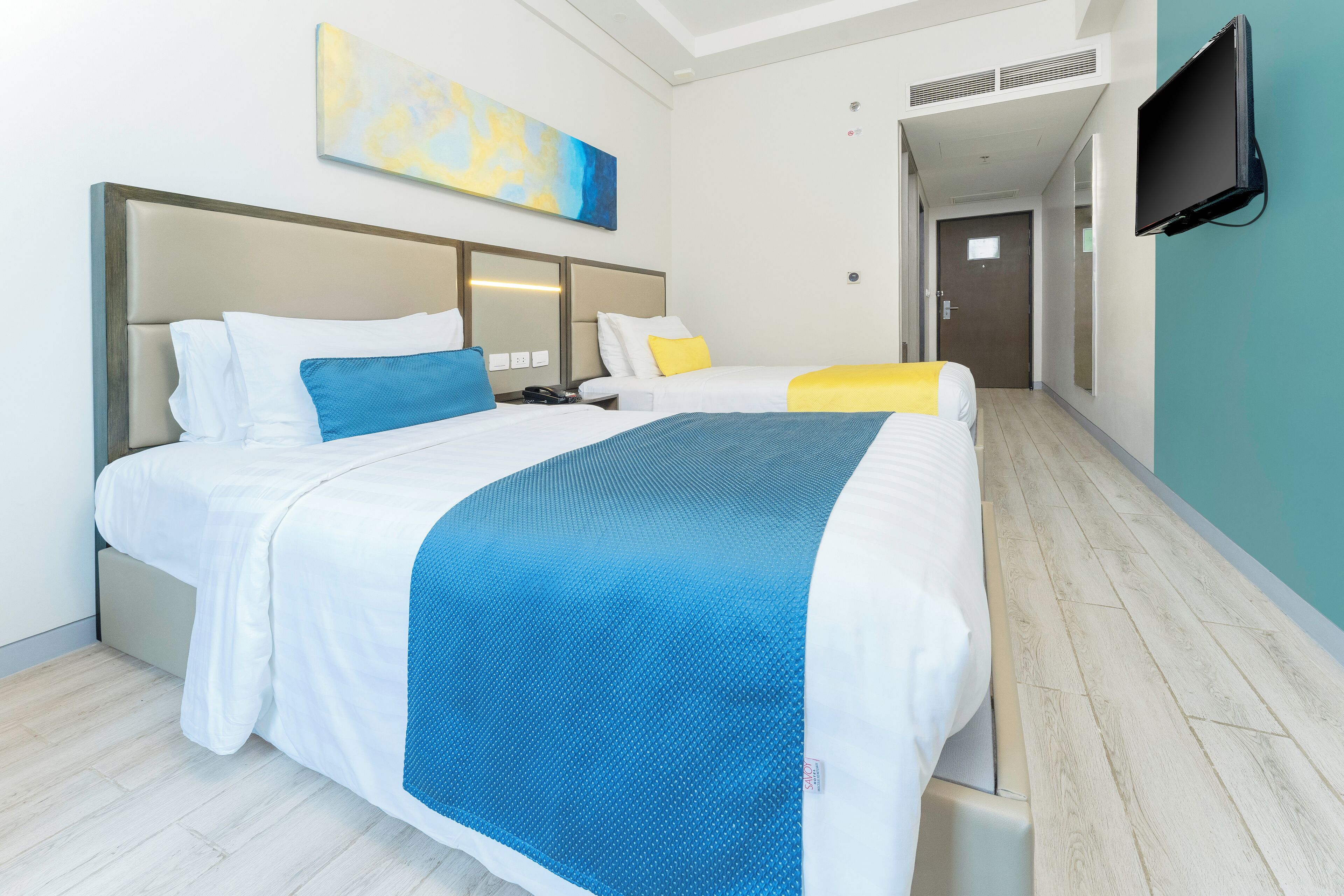 Quarto de hotel moderno com uma cama grande, televisão de tela plana na parede e um corredor que leva a outro quarto.