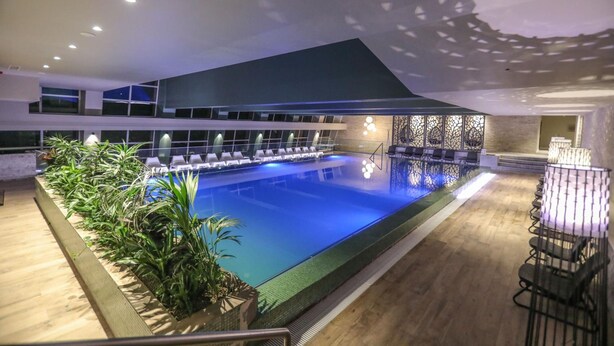 Piscina interior com espreguiçadeiras e um deque de madeira.